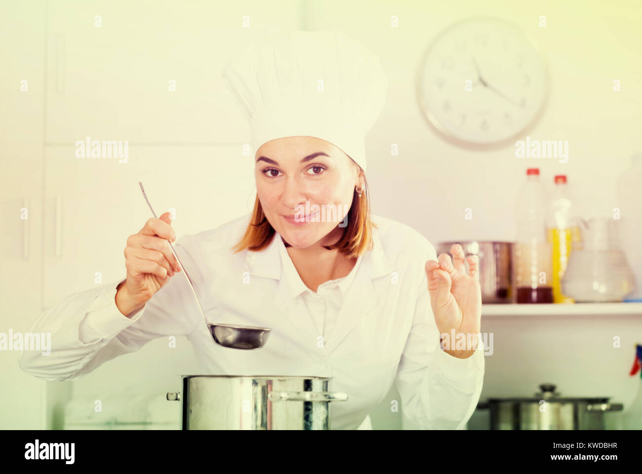 Smiling female cook checking taste of food while preparing in kitchen ...