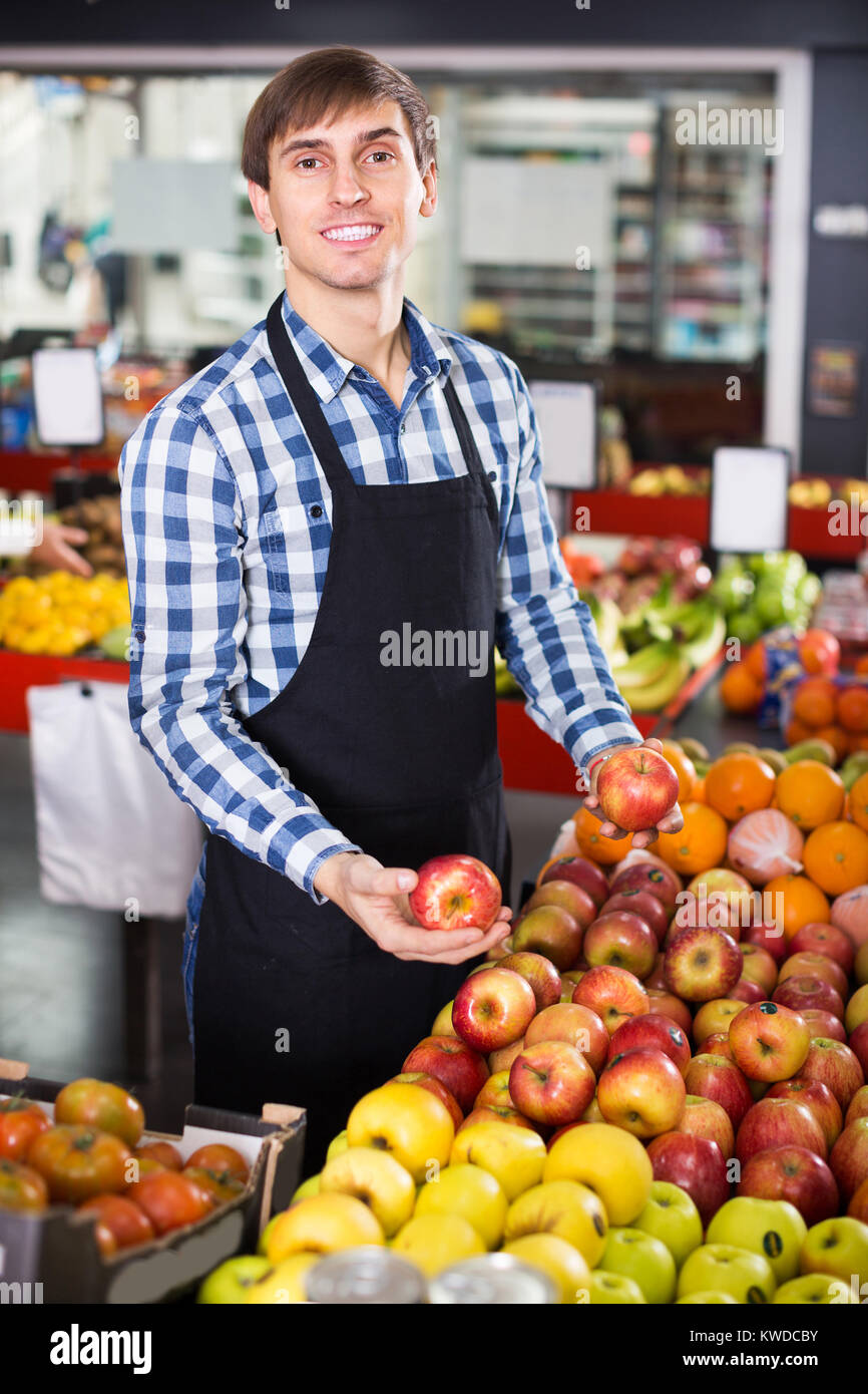 Positive grocery worker selling seasonal fruits in farm food store ...