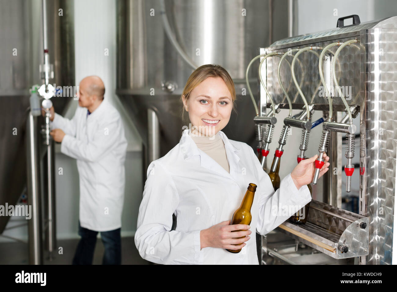 Young cheerful woman wearing uniform using bottling equipment on a ...