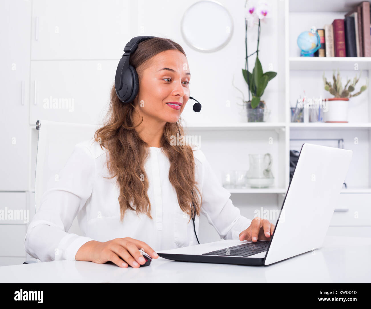 Smiling young woman talking with customer using hands-free set at ...