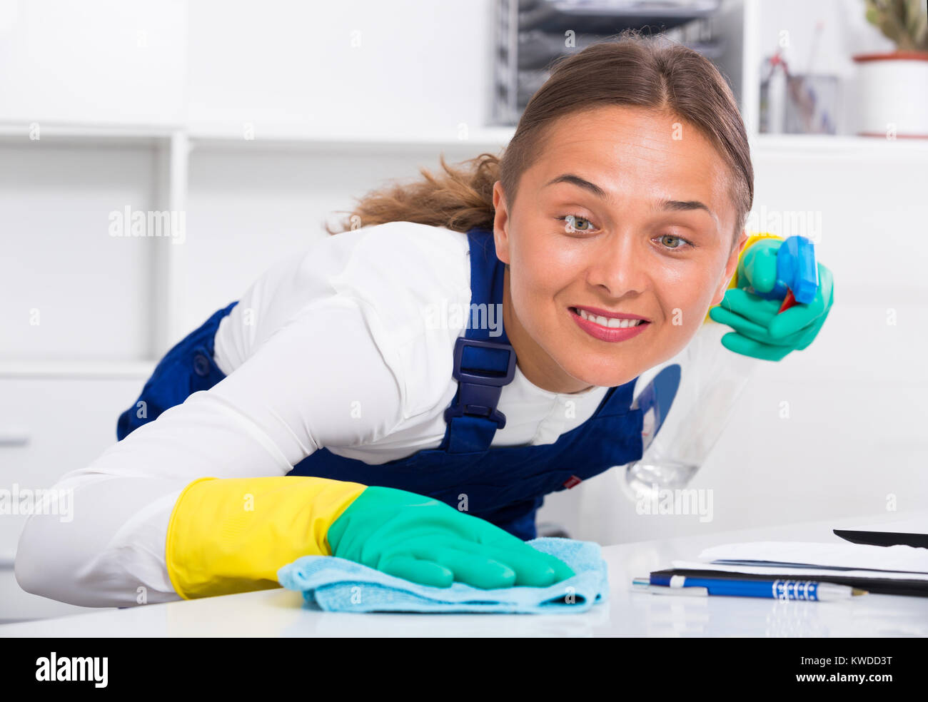 portrait of cheerful young female cleaner in uniform with duster at ...
