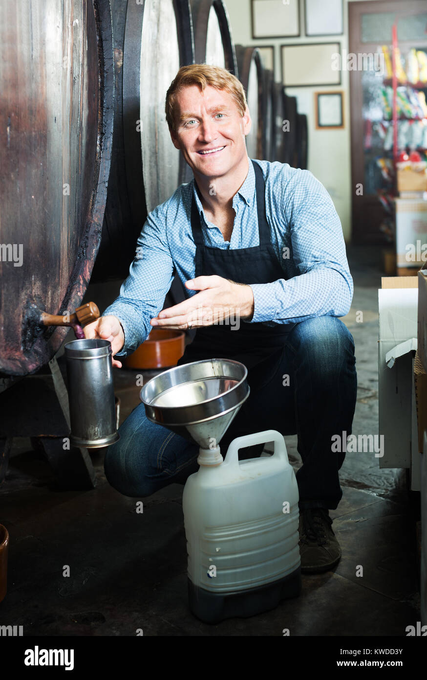 Portrait of positive male seller wearing uniform pouring liquor from ...