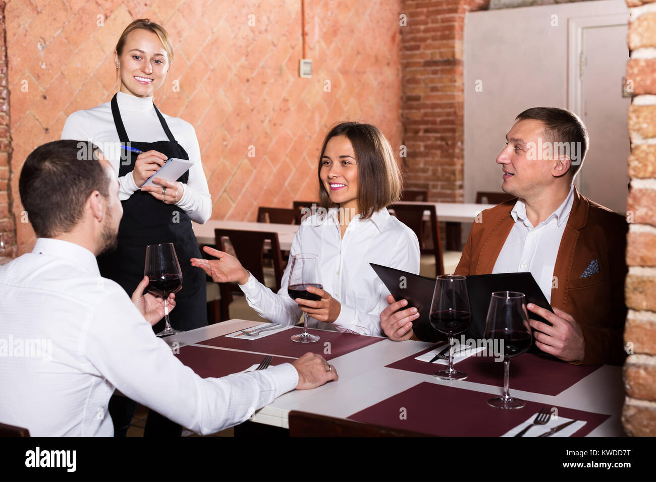 Smiling female waiter taking order from visitors in country restaurant ...