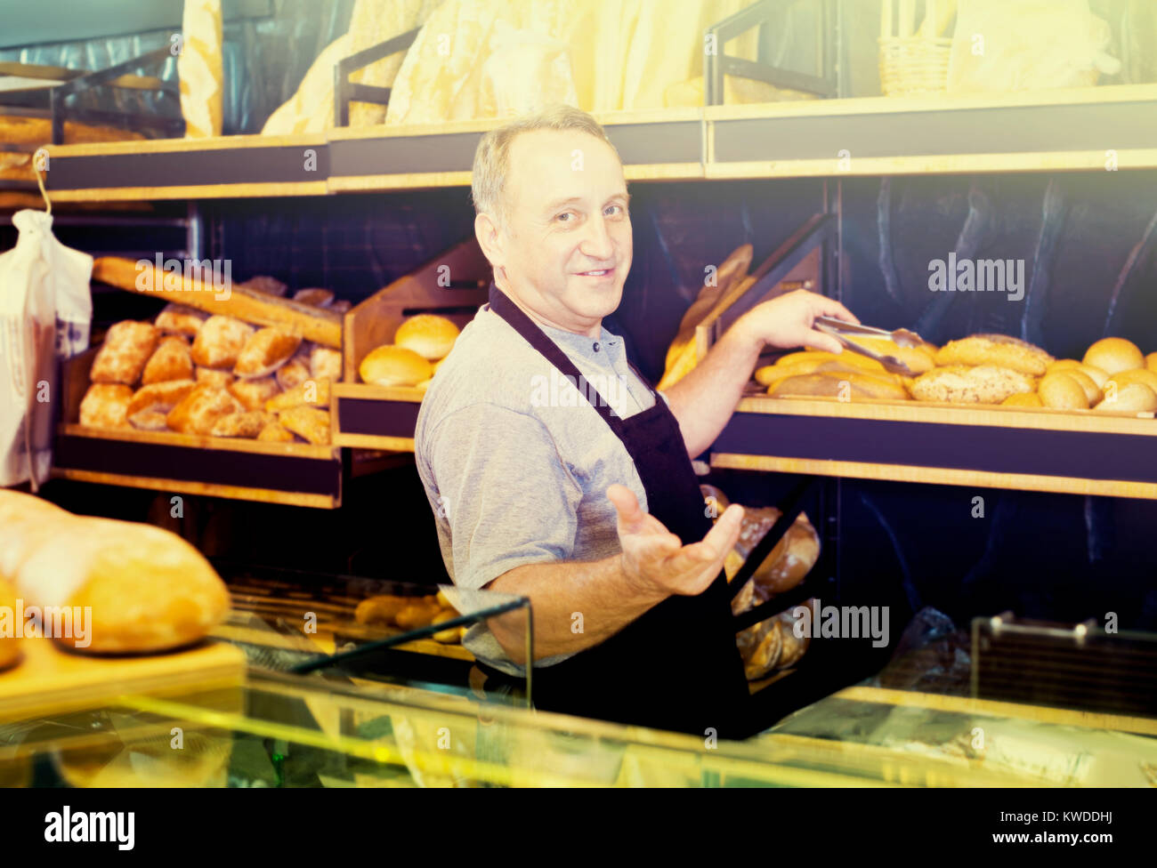 Mature man baker offering fresh baguettes and buns in bakery Stock ...