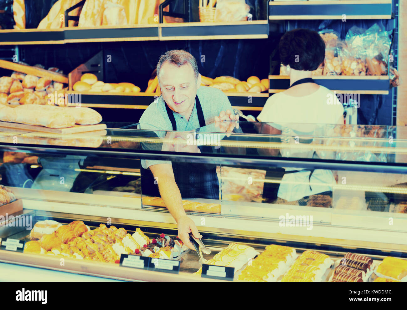 Smiling mature man with sweet confectionery products on counter of ...