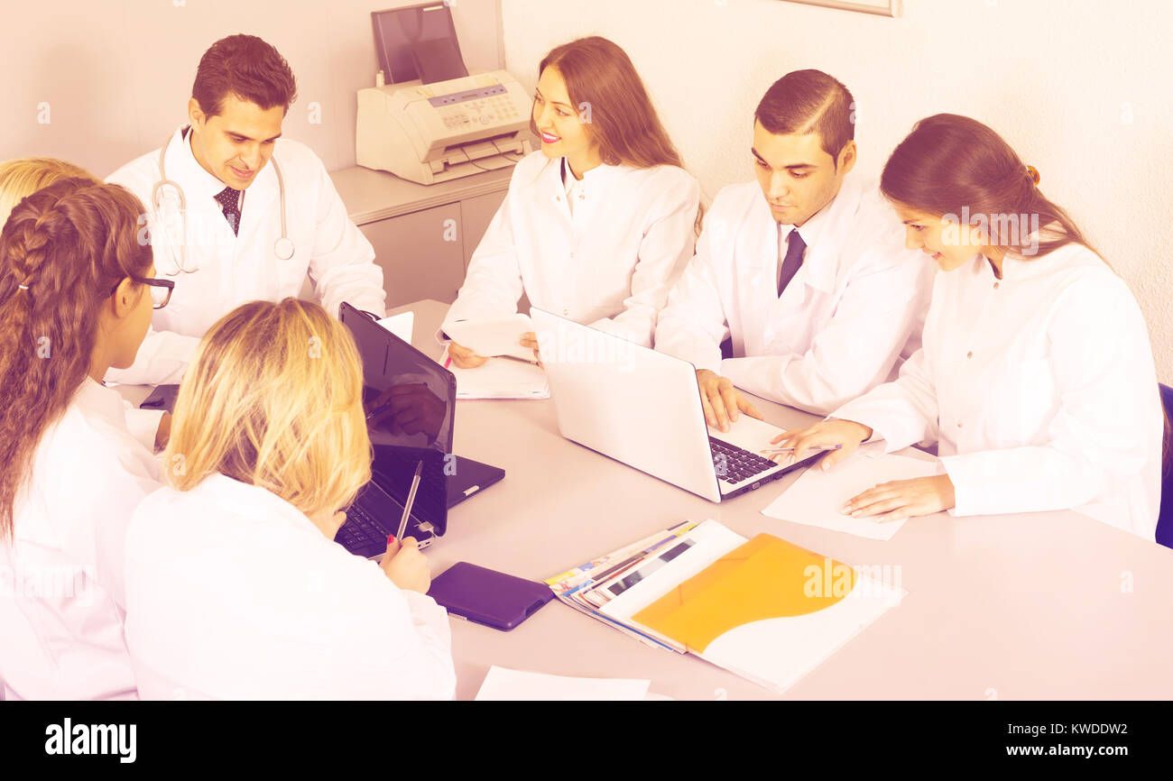 Group of young scientists in white overalls having discussion of ...