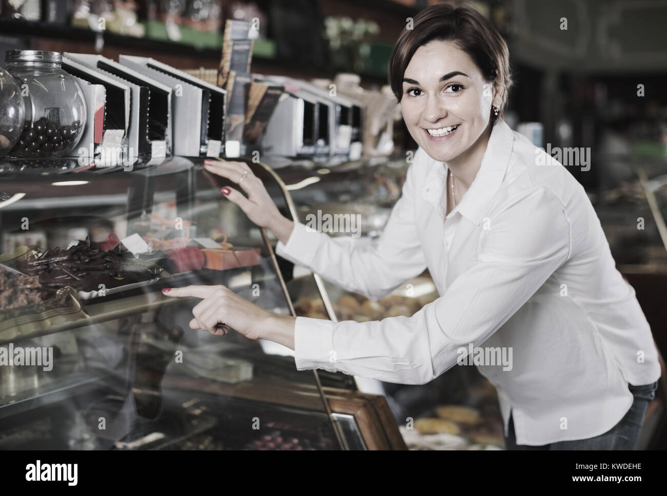 Young cheerful positive female customer examining desserts in ...