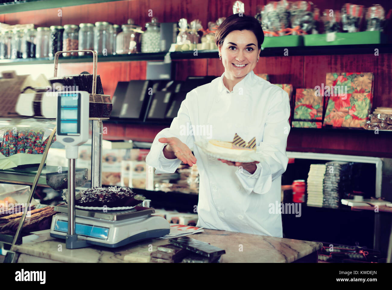 Young female seller offering sweet pie with icing in confectionery ...