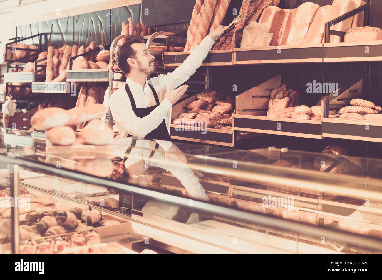 Smiling male seller offering fresh loaf of bread in bakery Stock Photo ...