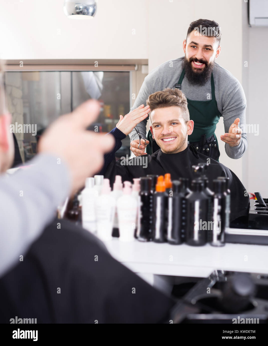 Smiling client describing his desirable haircut to hairdresser at hair ...