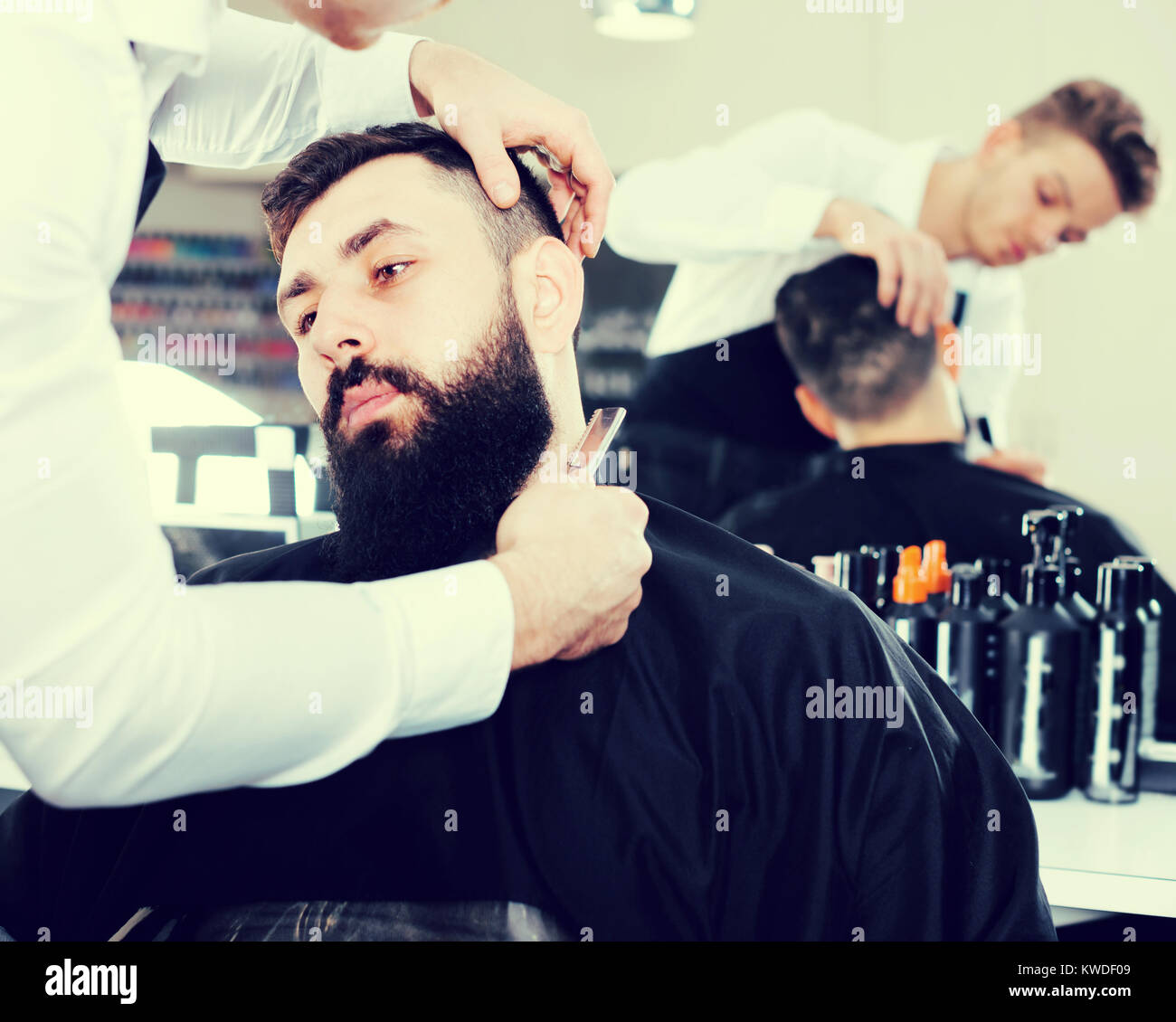 Adult stylist creating new shape for beard of client at hairdressing ...