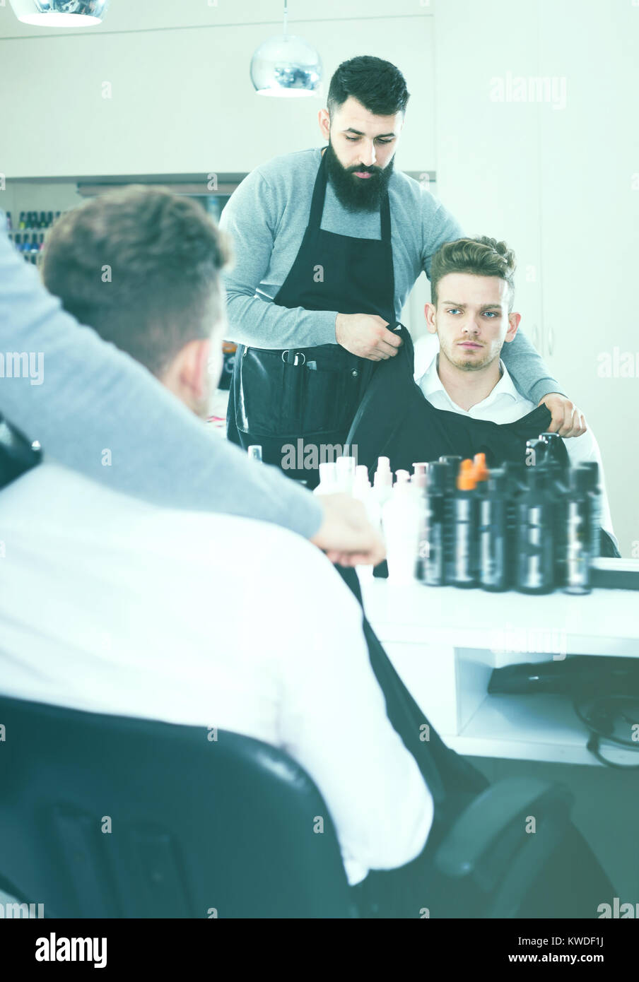 Man making client comfortable before haircut at salon Stock Photo - Alamy