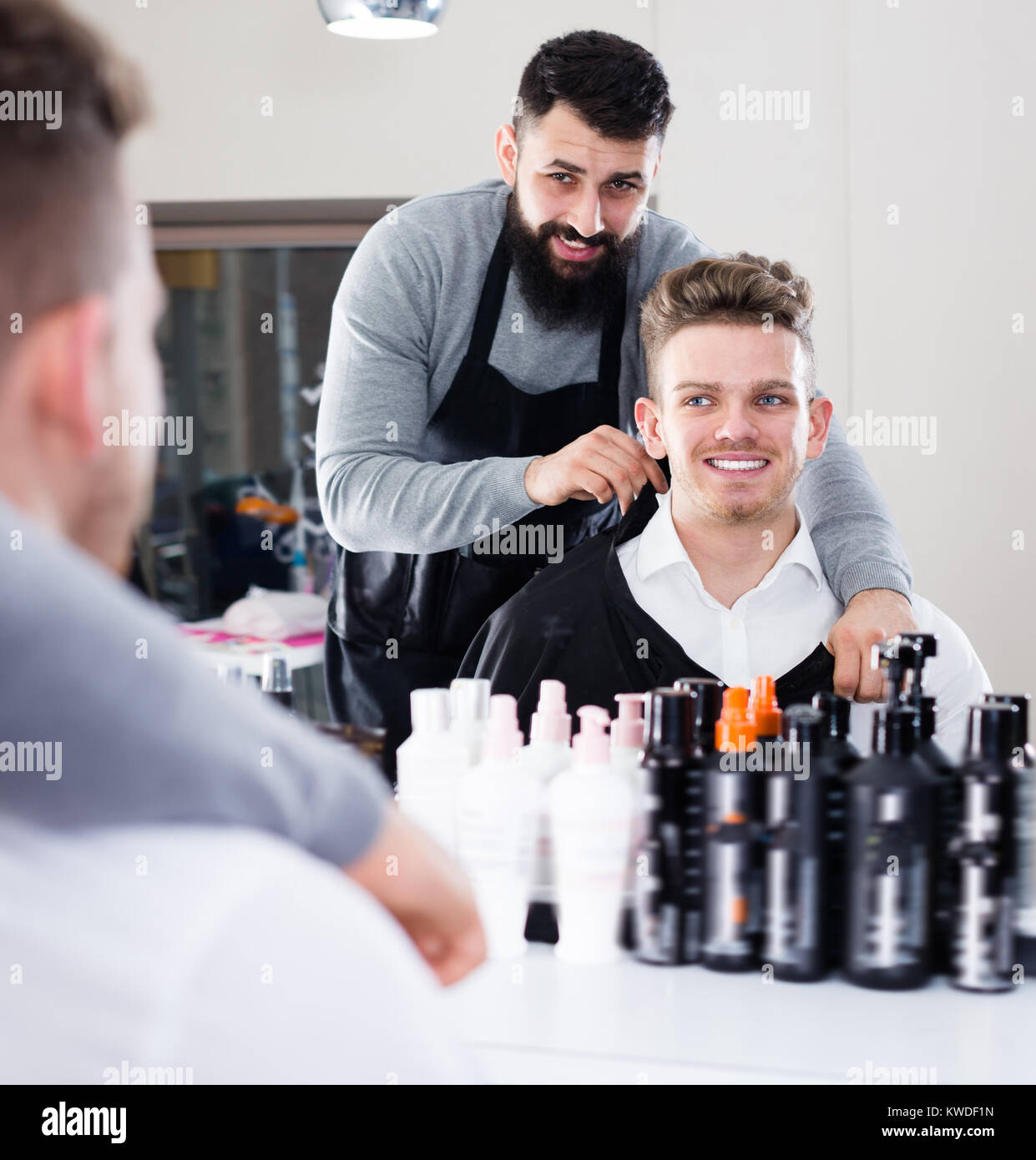Cheerful hairdresser making client comfortable before haircut at salon ...