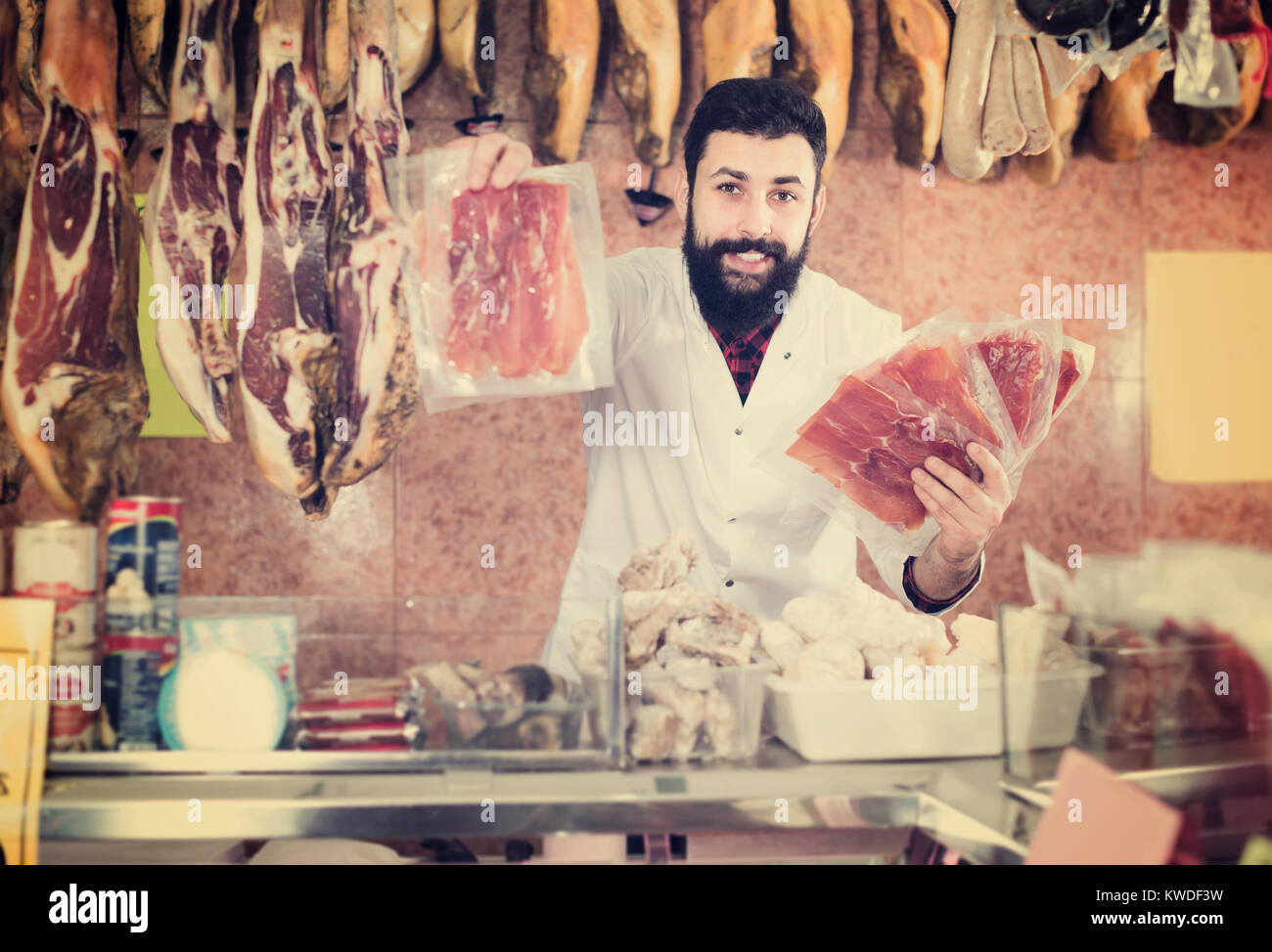 Positive man seller showing sliced prosciutto in butcher’s store Stock ...