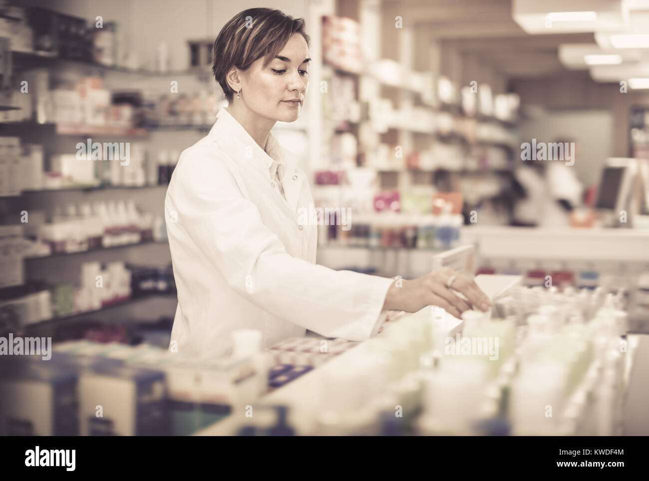Adult female pharmacist arranging assortment of products in pharmacy ...