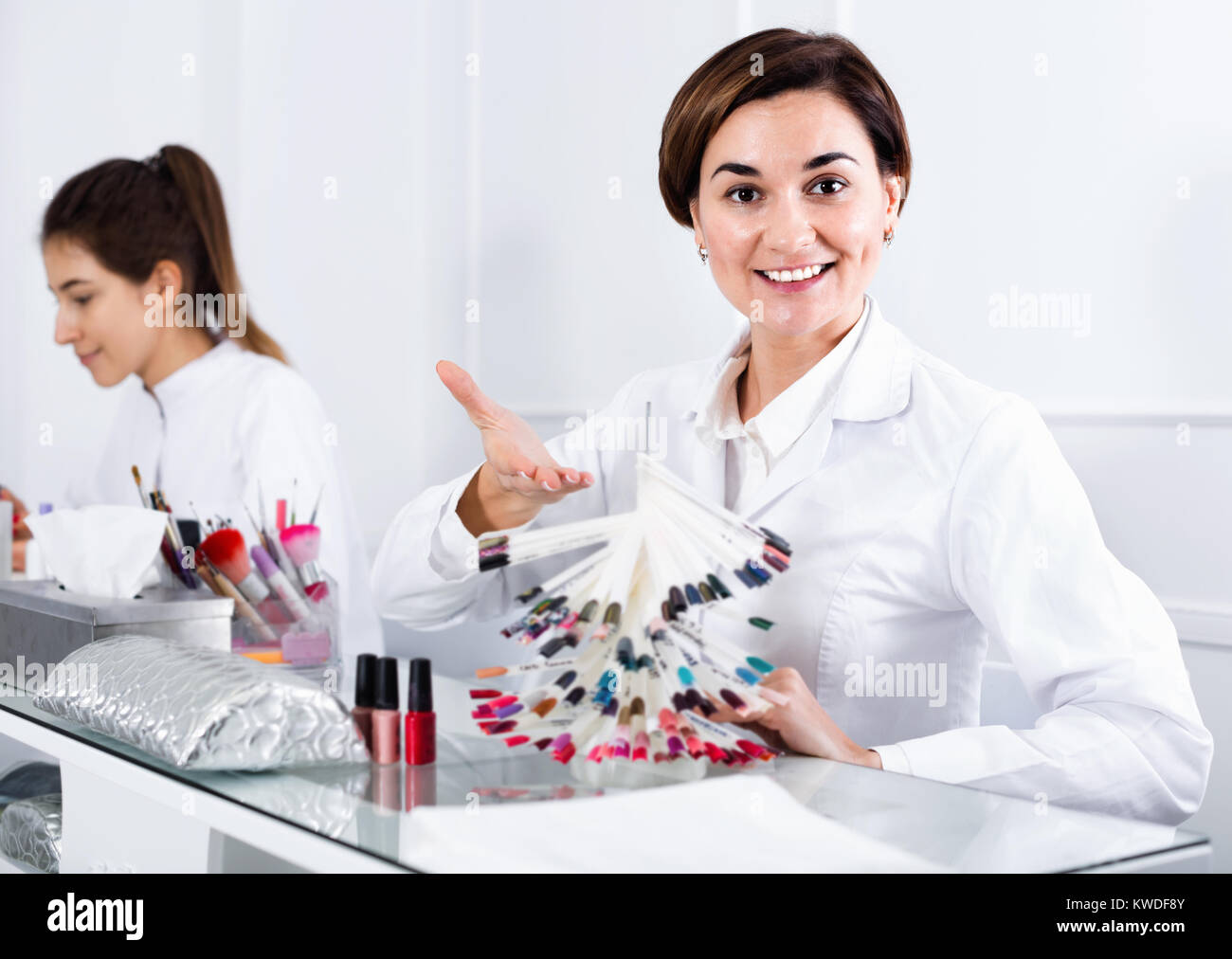 Satisfied female manicurist showing lacquer color schemes in nail salon ...