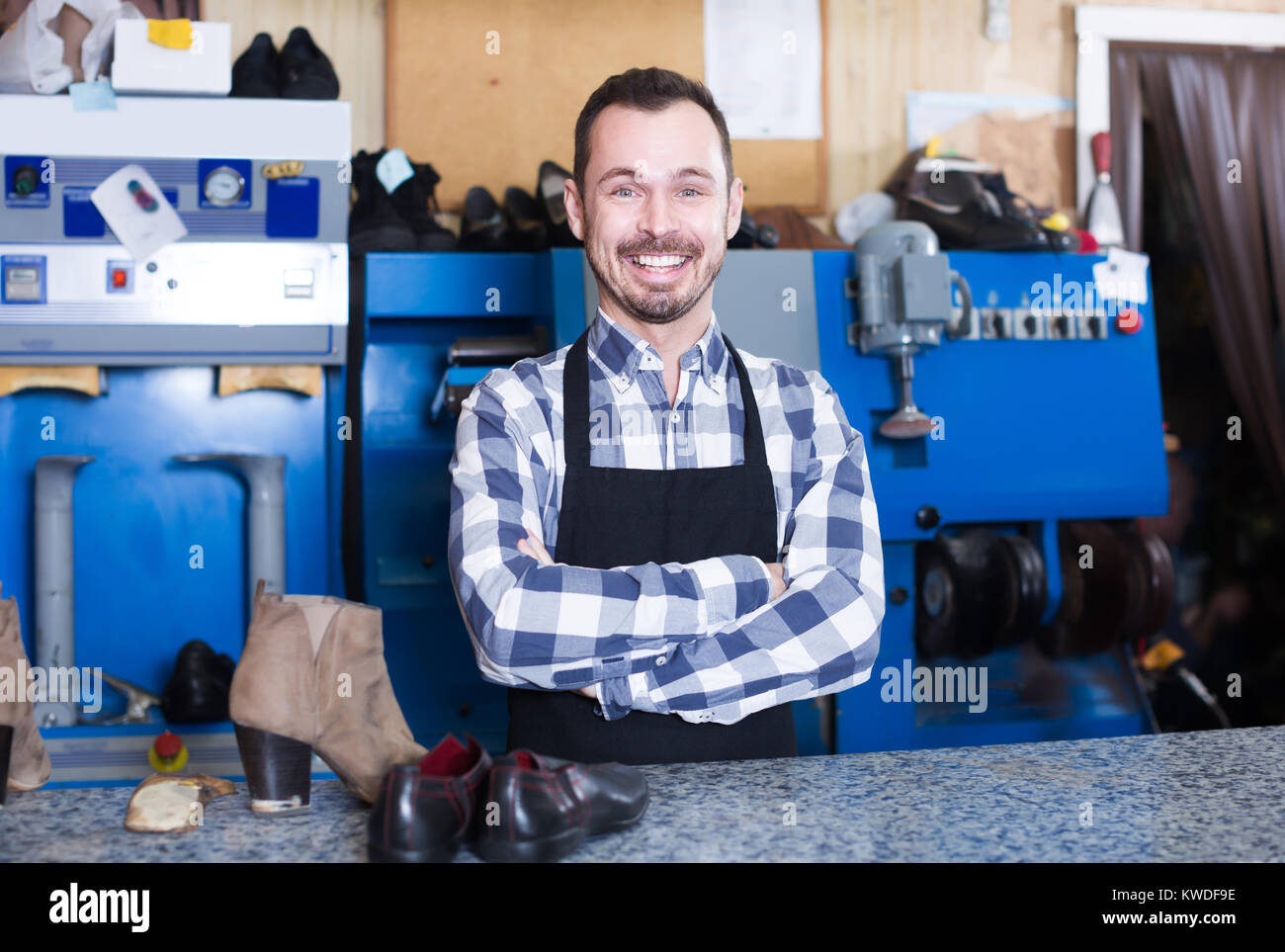 Positive male worker showing his workplace and tools in shoe repair ...