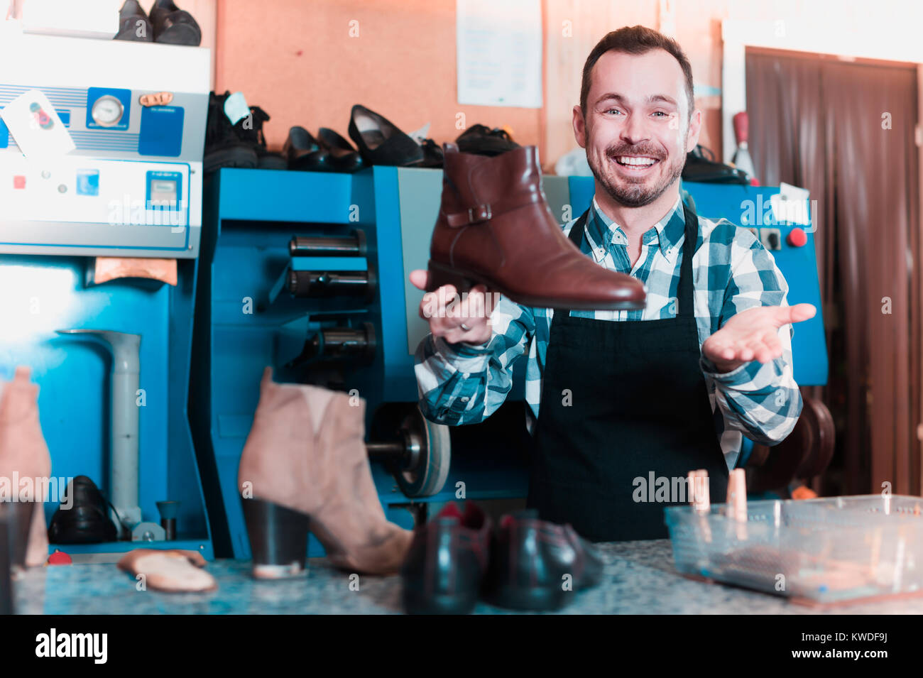 Glad male worker showing fixed shoes in shoe repair workshop Stock ...