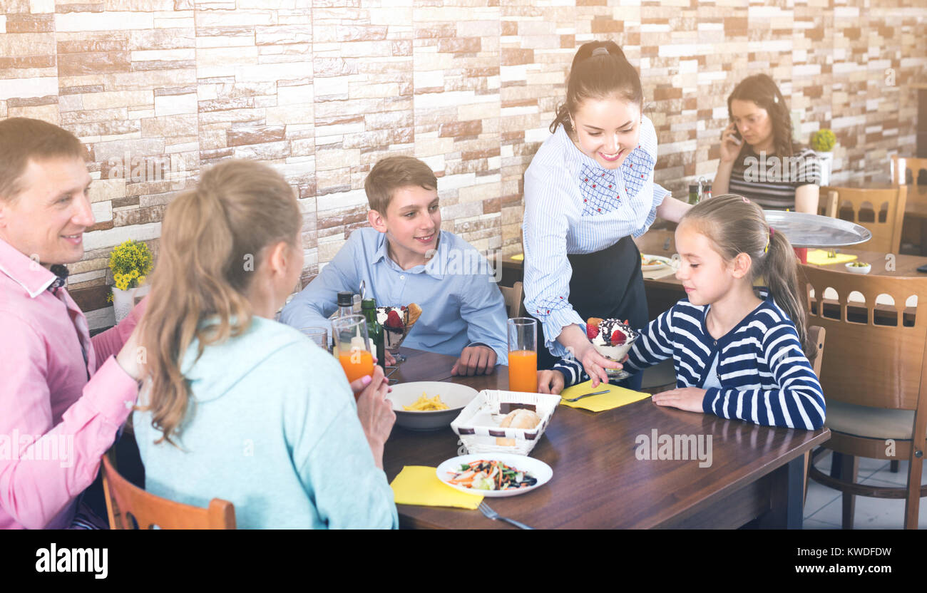 Girl is bringing delicious dessert to young visitors of family cafe ...