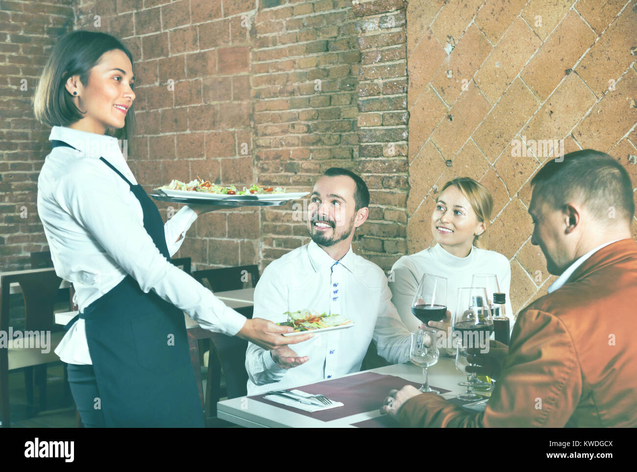 Pleasant cheerful female waiter bringing order to visitors in country ...