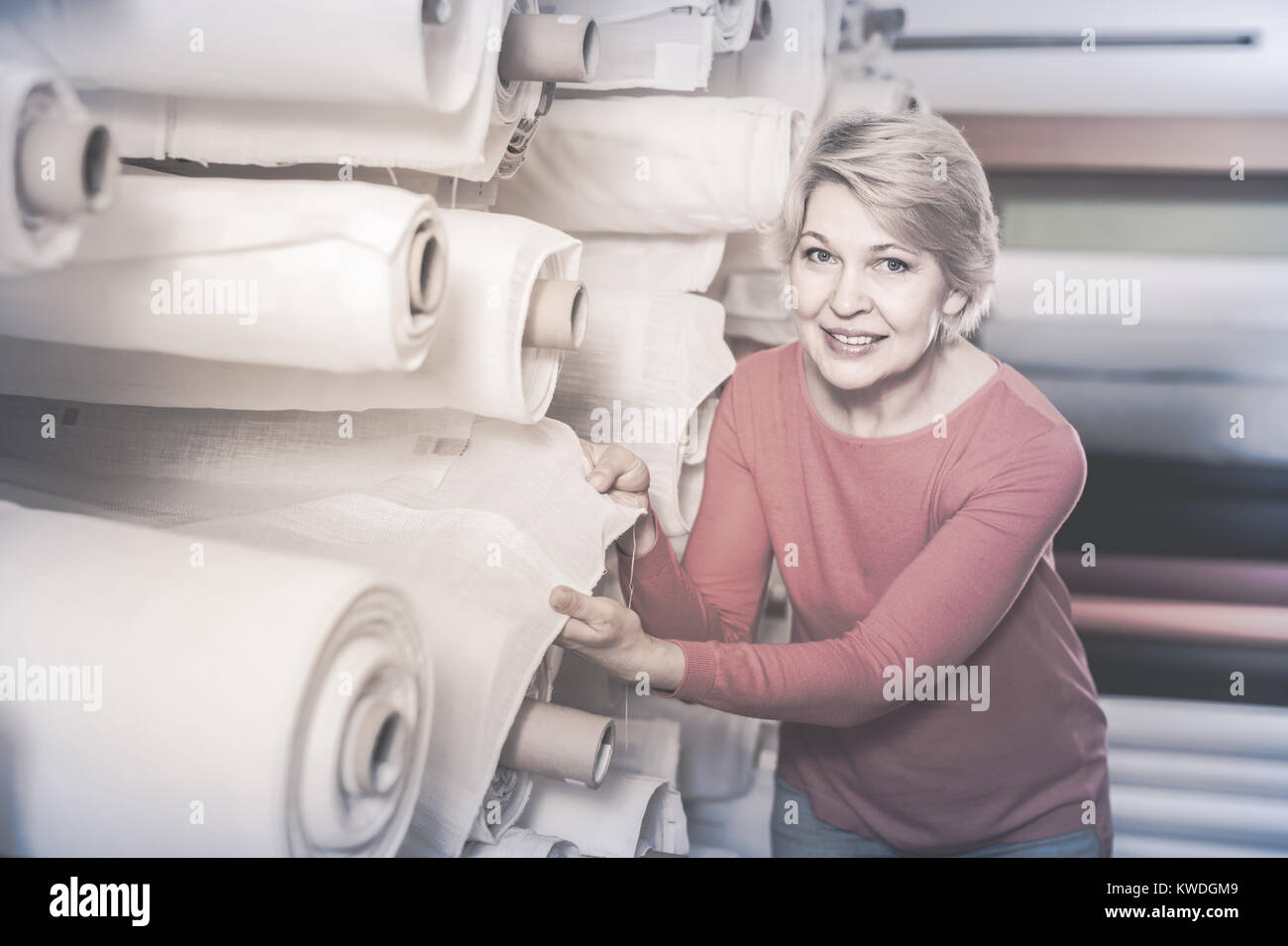 Positive woman choosing interesting fabric in textile shop Stock Photo ...