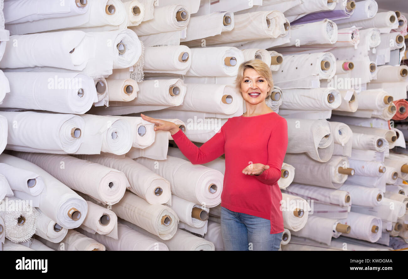 smiling female shop assistant demonstrating assortment at textile shop ...