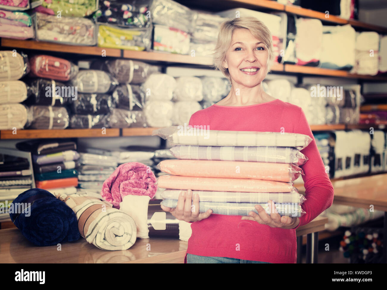 Smiling senior seller is showing wide assortment of bed linen in a ...
