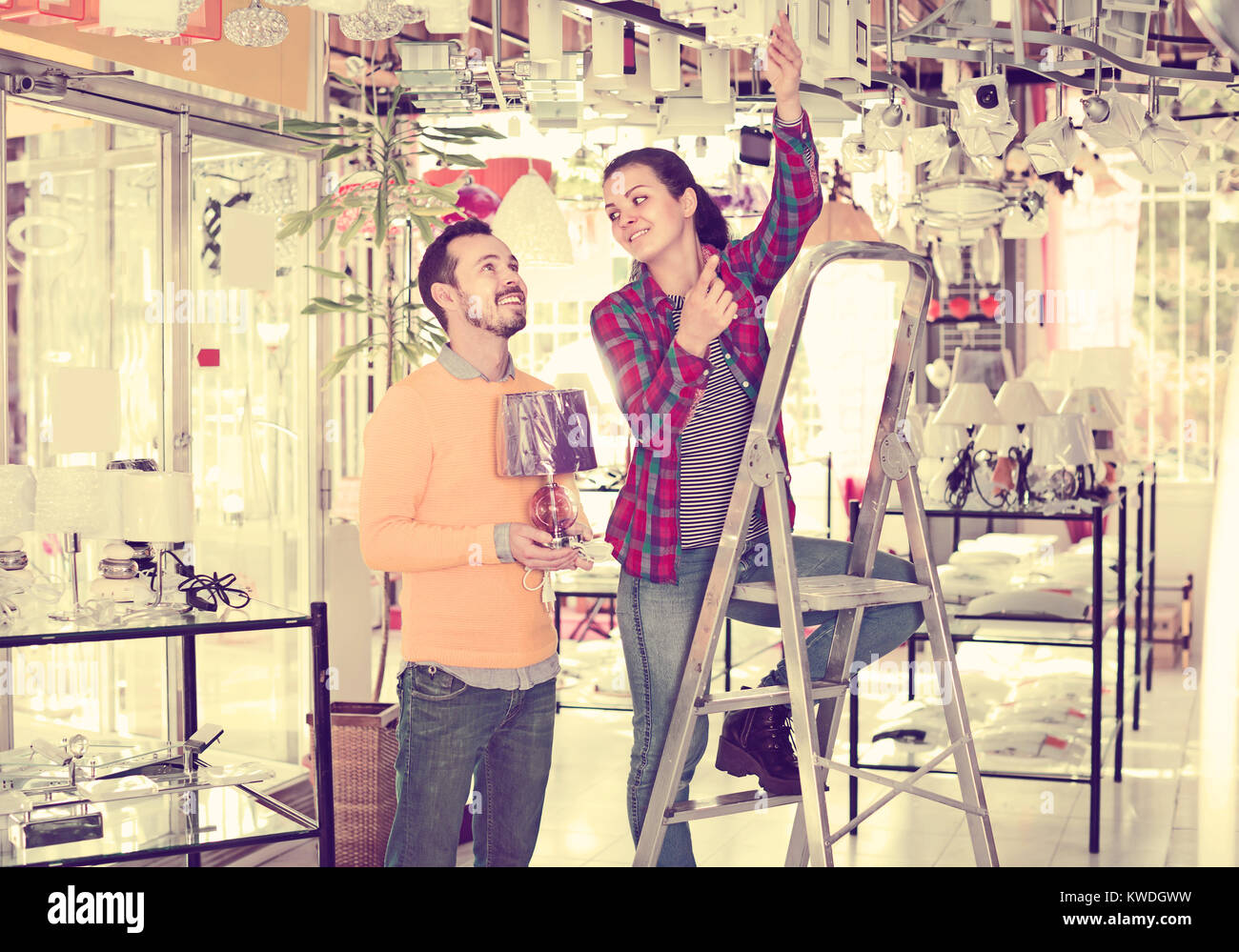 Young man and girl in lighter shop choosing modern glass pendant lamp ...
