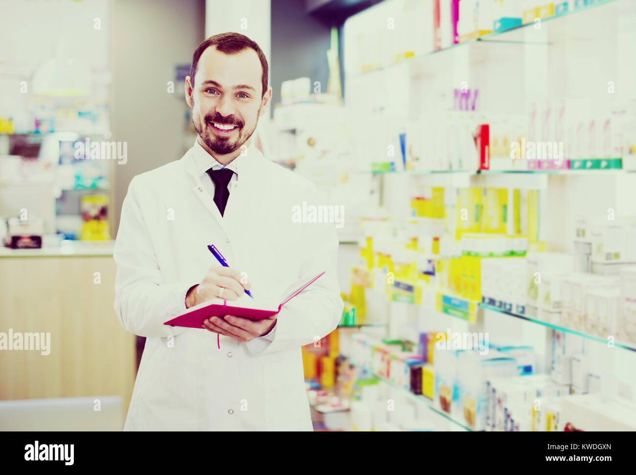 Young positive male pharmacist checking assortment of drugs in pharmacy ...
