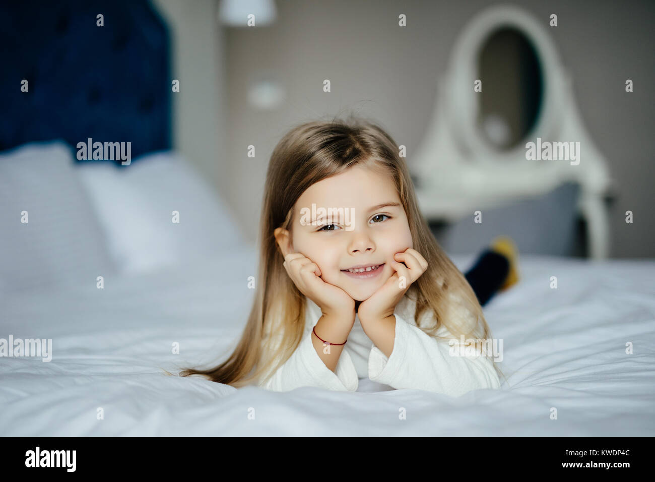 Close-up portrait of beautiful little kid lying on bed with hand under ...