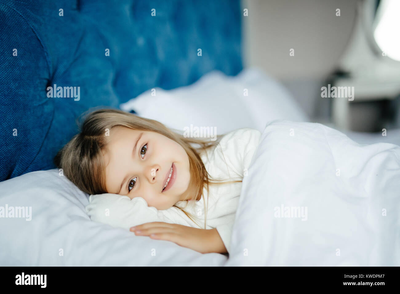 Close-up portrait of beautiful little kid lying on bed with hand under ...