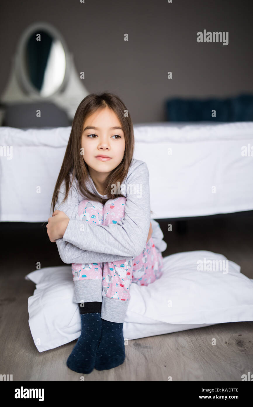 Portrait of an upset little girl sitting on the floor near bed and ...