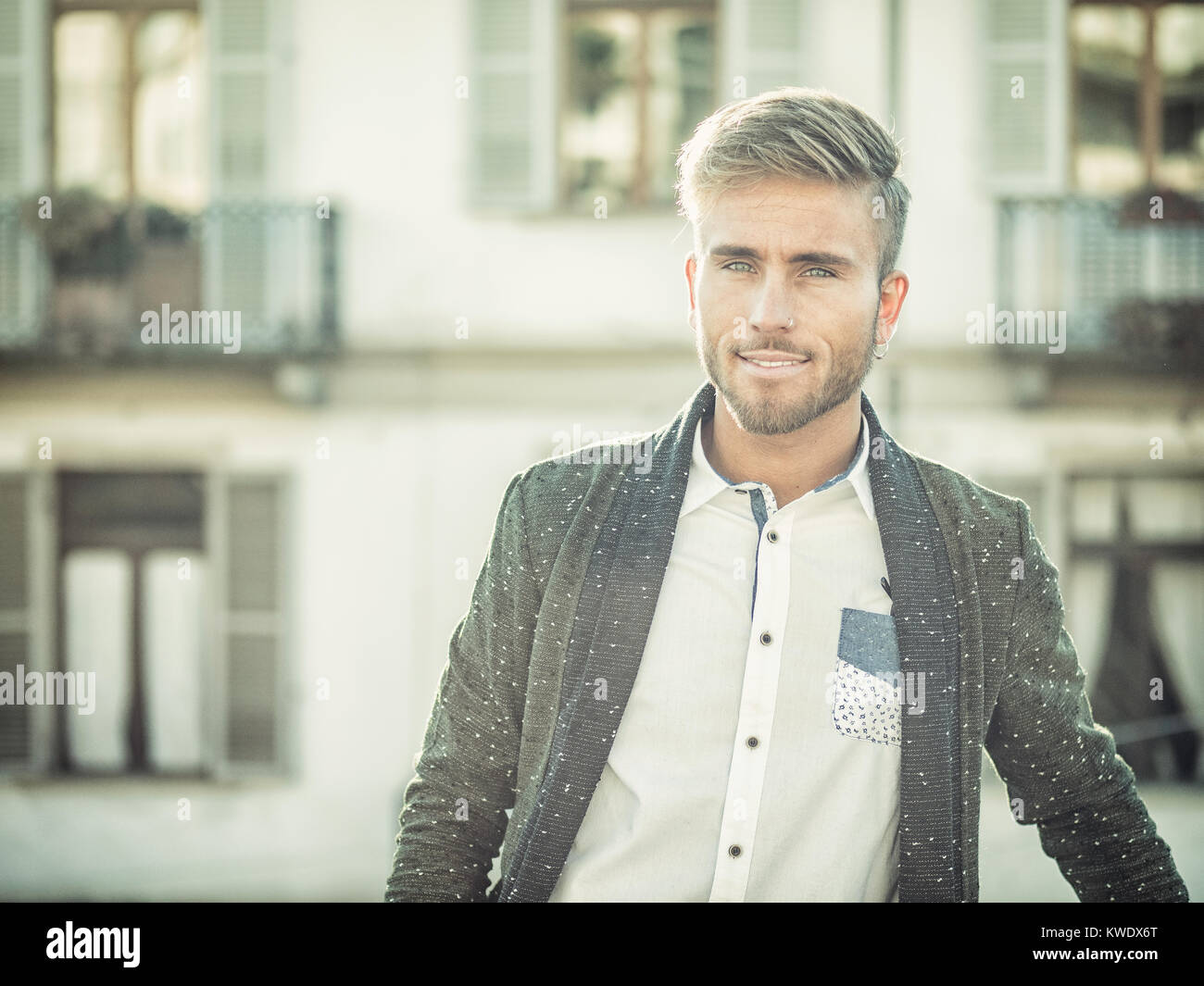 Handsome trendy blond man standing outdoor in European city setting ...
