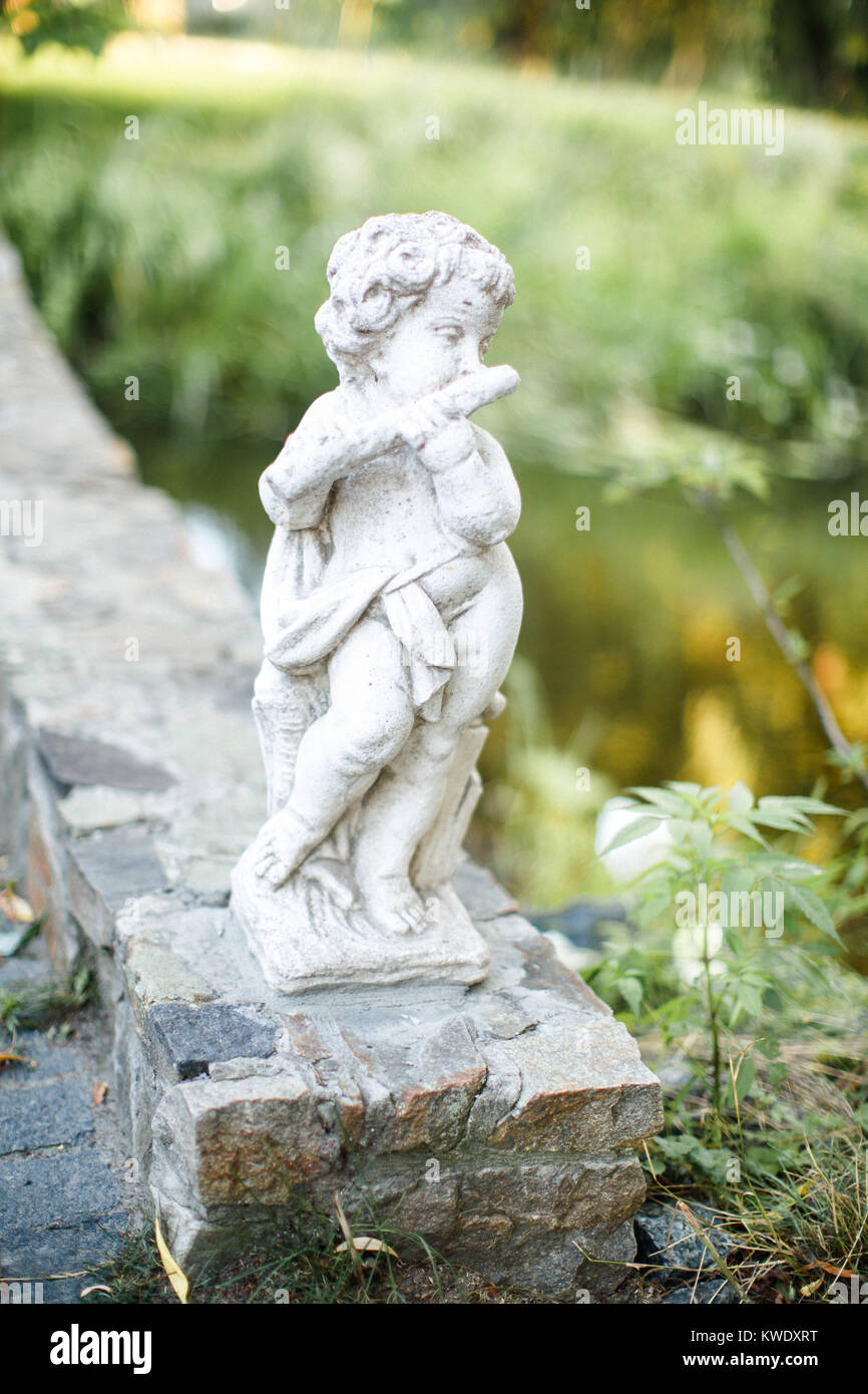 The cute stone statue playing flute instrument in the garden. Angel ...
