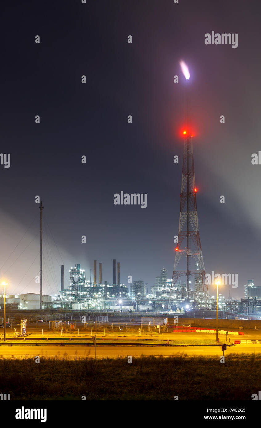 A tall flare stack in an oil refinery in the harbor of Antwerp at night ...