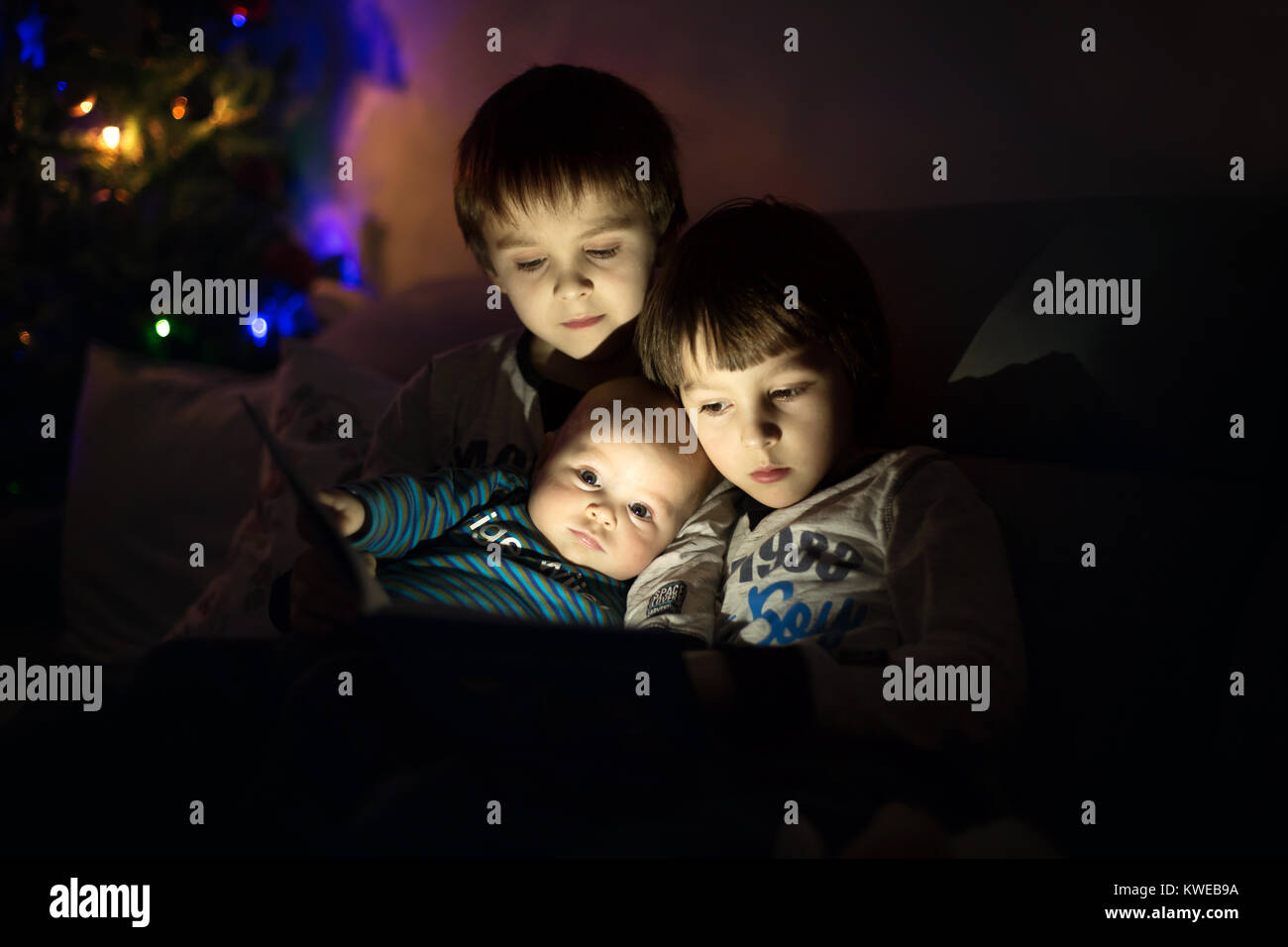 Three brothers, sitting at home on sofa in living room, reading a book ...