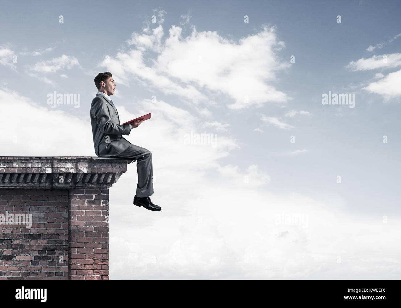 Man on roof edge reading book and cloudscape at background Stock Photo ...