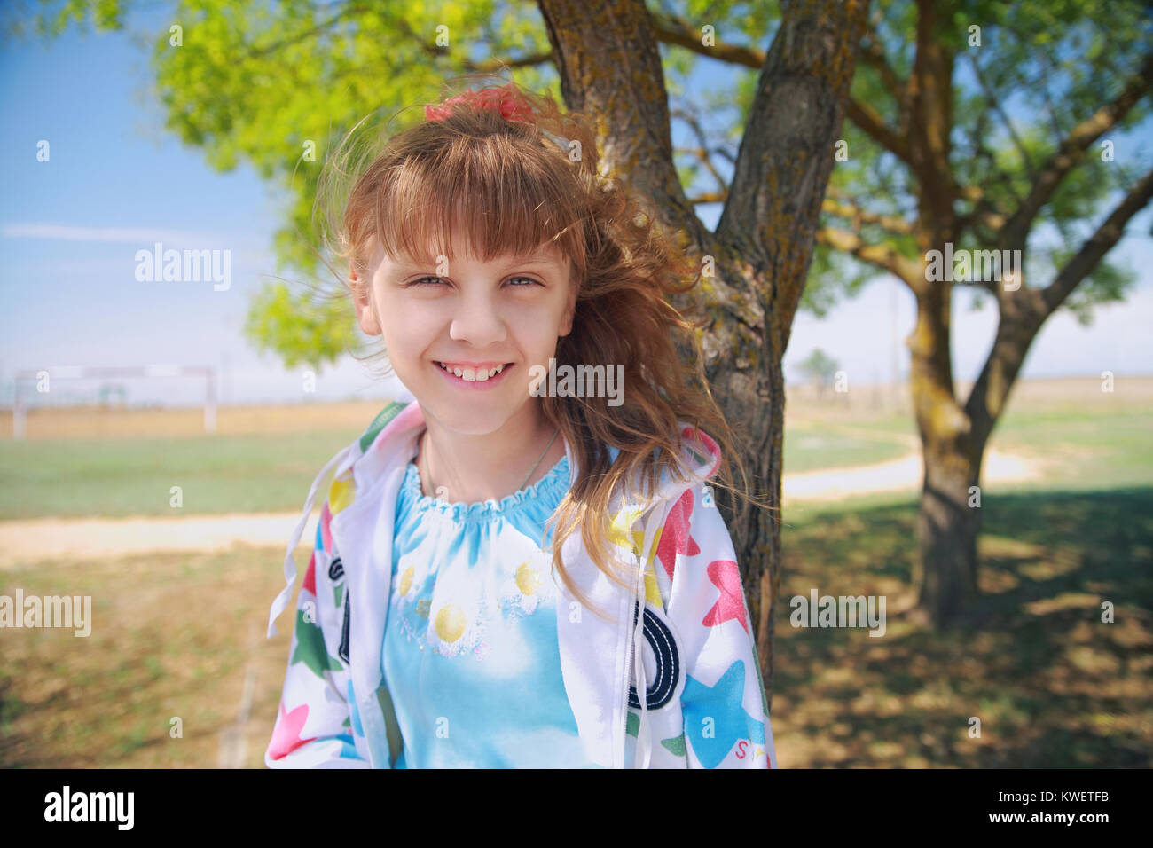 Little girl in the nature sitting under a tree, smiling and looking at ...