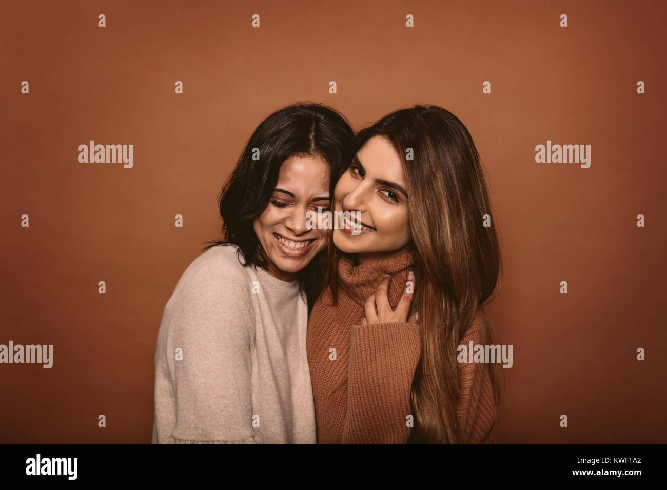 Two young woman standing together in studio and smiling. Happy female ...