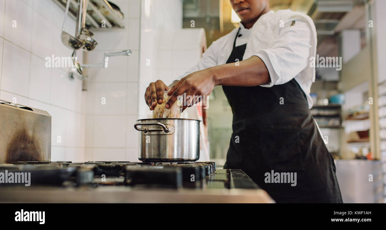 Chef adding food ingredients in stainless steel pot on stove. Cropped ...
