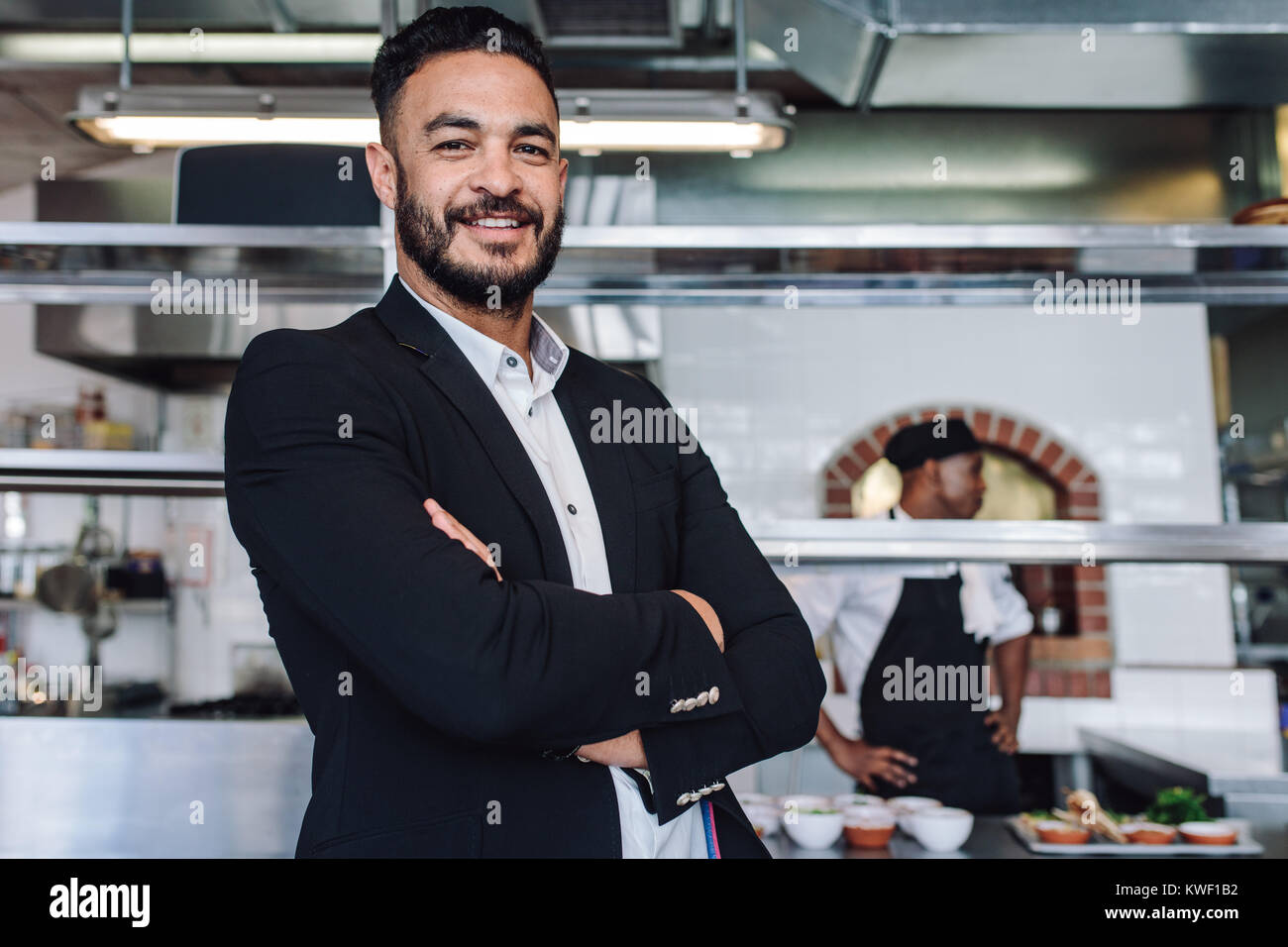 Portrait of young businessman standing in his restaurant with staff in ...