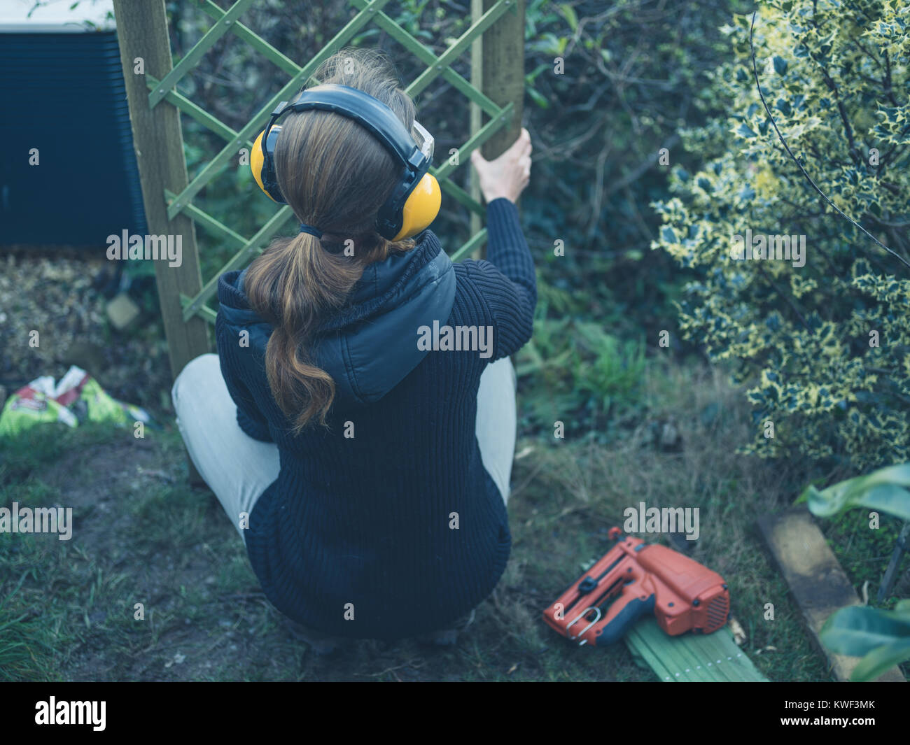 A young woman wearing ear muffs is building a fence in her garden Stock ...
