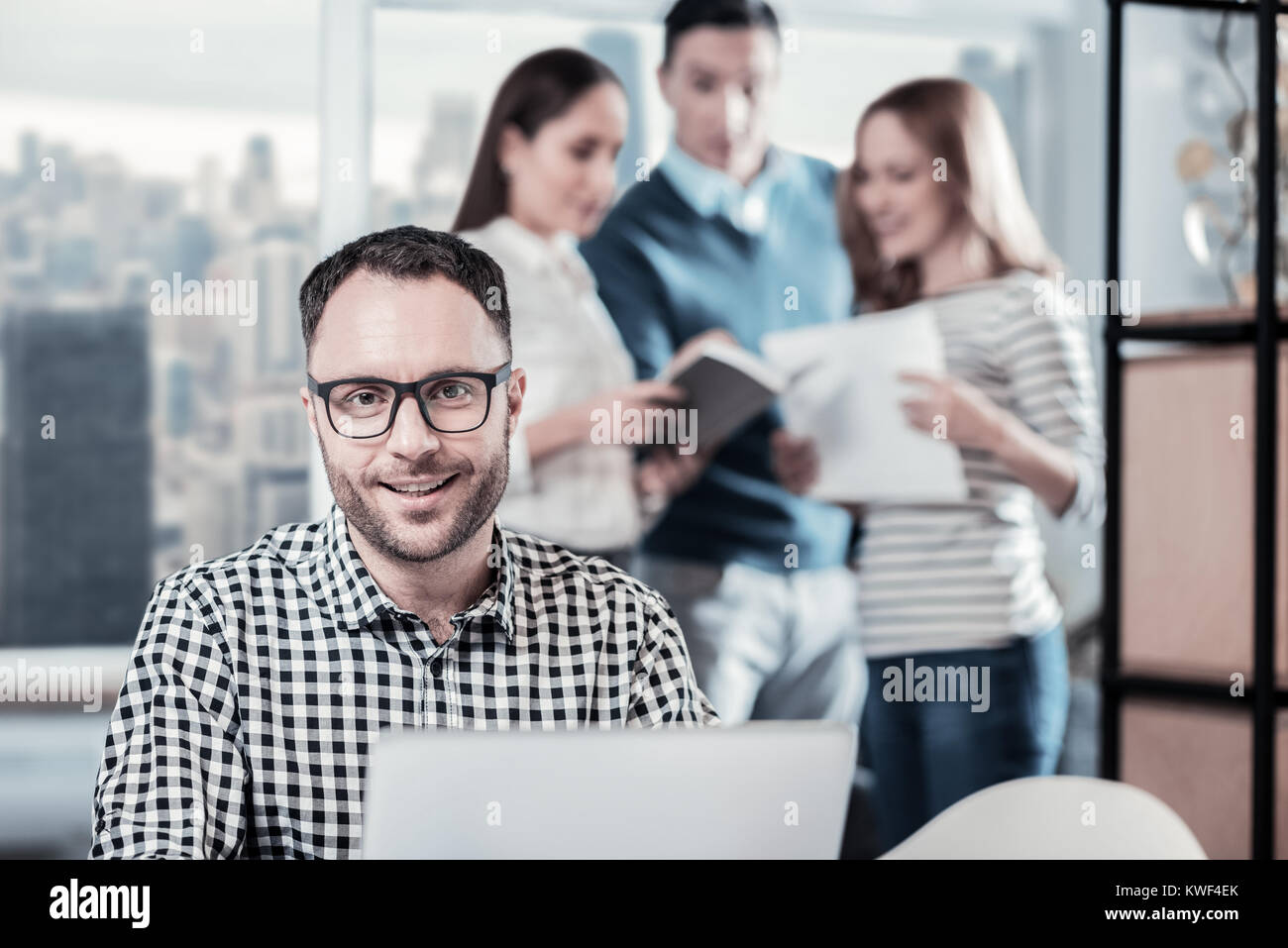 Calm work. Handsome smiling pleasant man sitting in the office looking ...