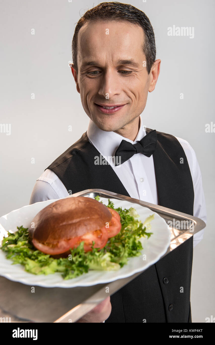 Perfect sandwich. Merry vigorous male waiter staring at salver while ...