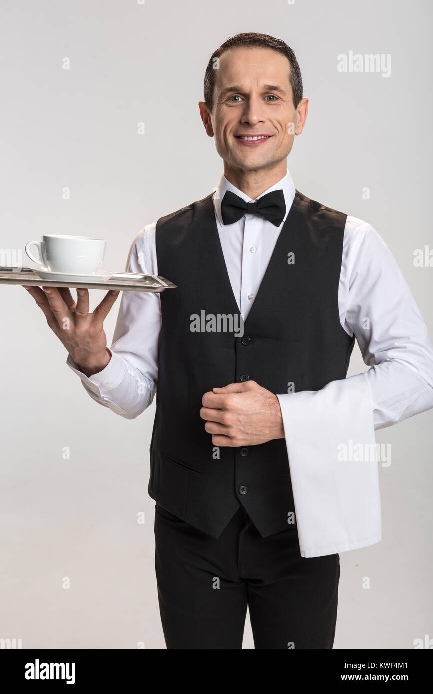 Your tea. Attractive vigorous male waiter standing on the grey ...