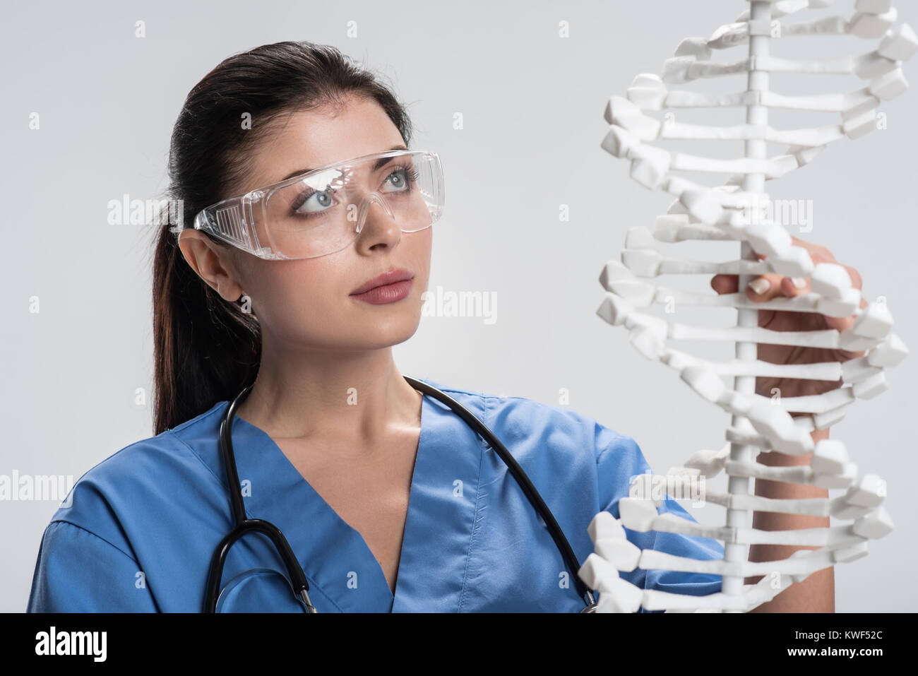 Genetic secret. Musing young female doctor tipping DNA model while ...