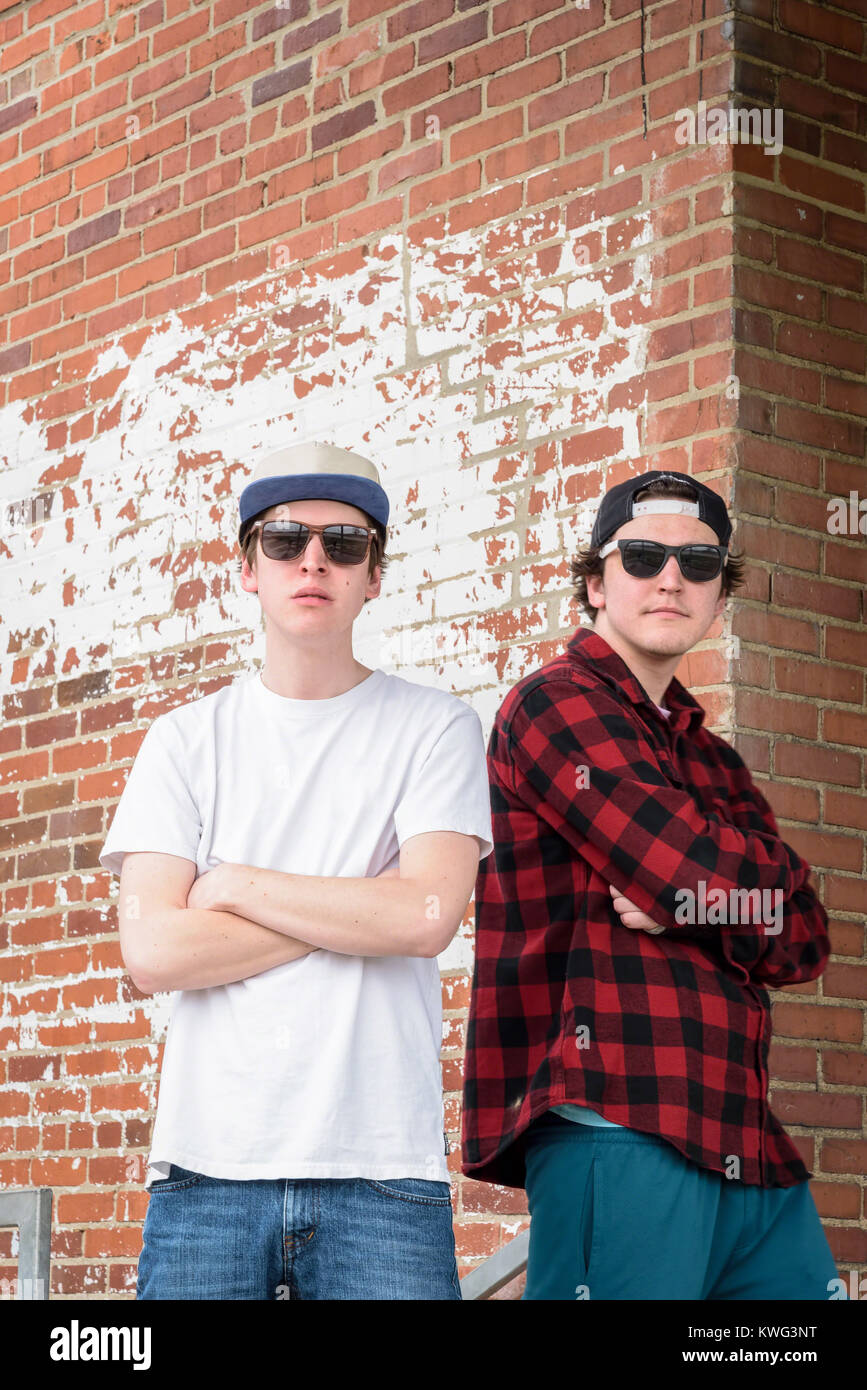 two young men wearing sunglasses and hats standing back to back with ...