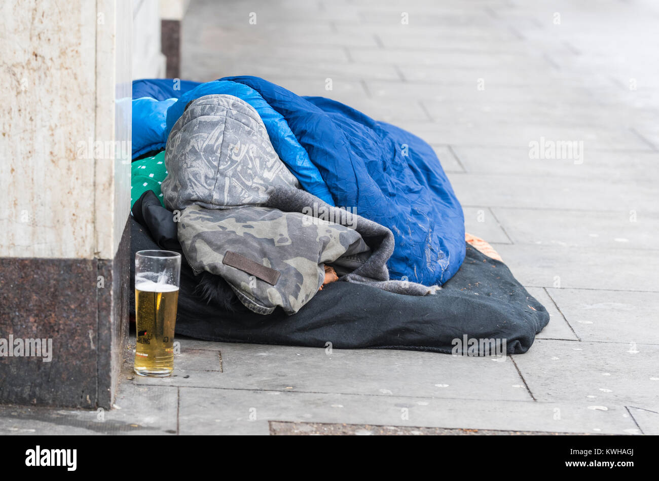 Homeless person sleeping on the streets with a partially drunk cup of ...