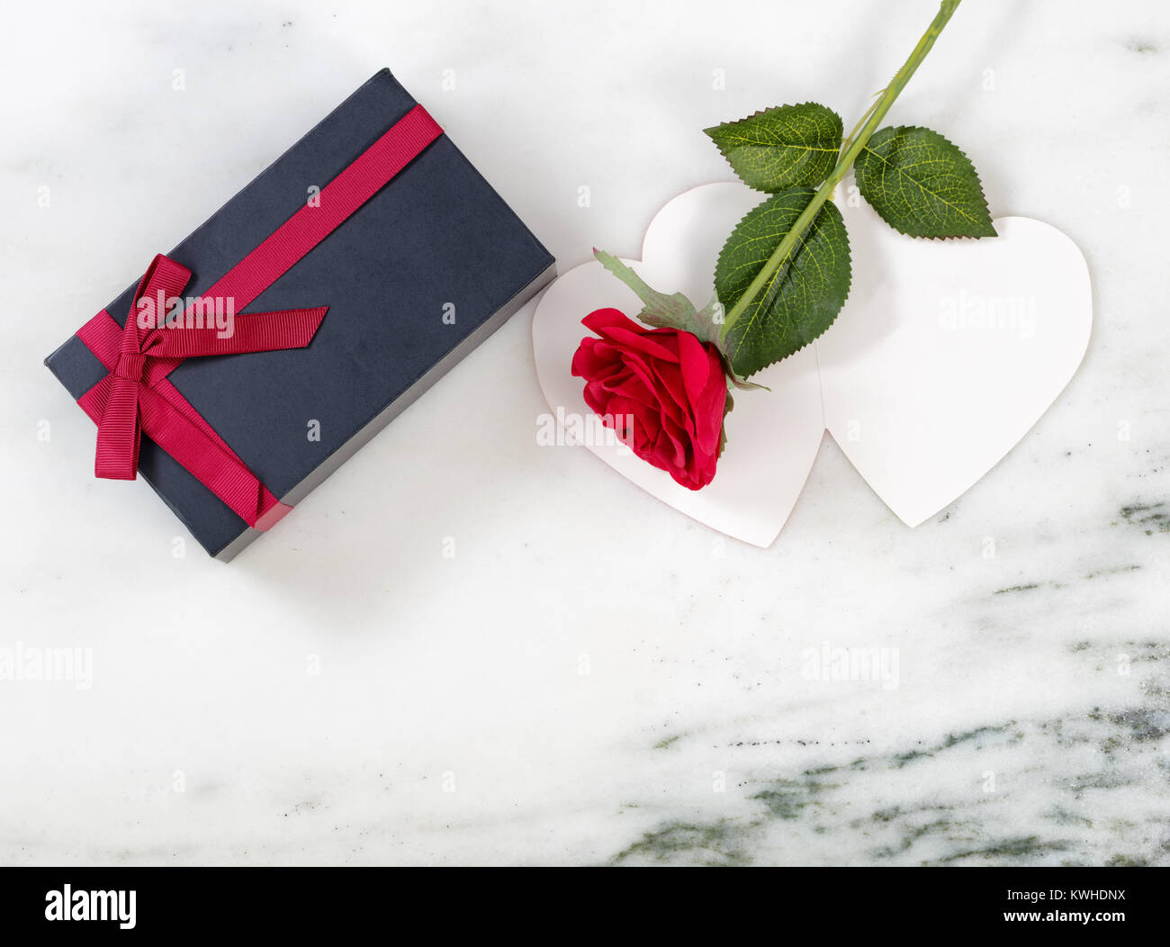 Single red rose on card with dark gift box on marble stone background ...