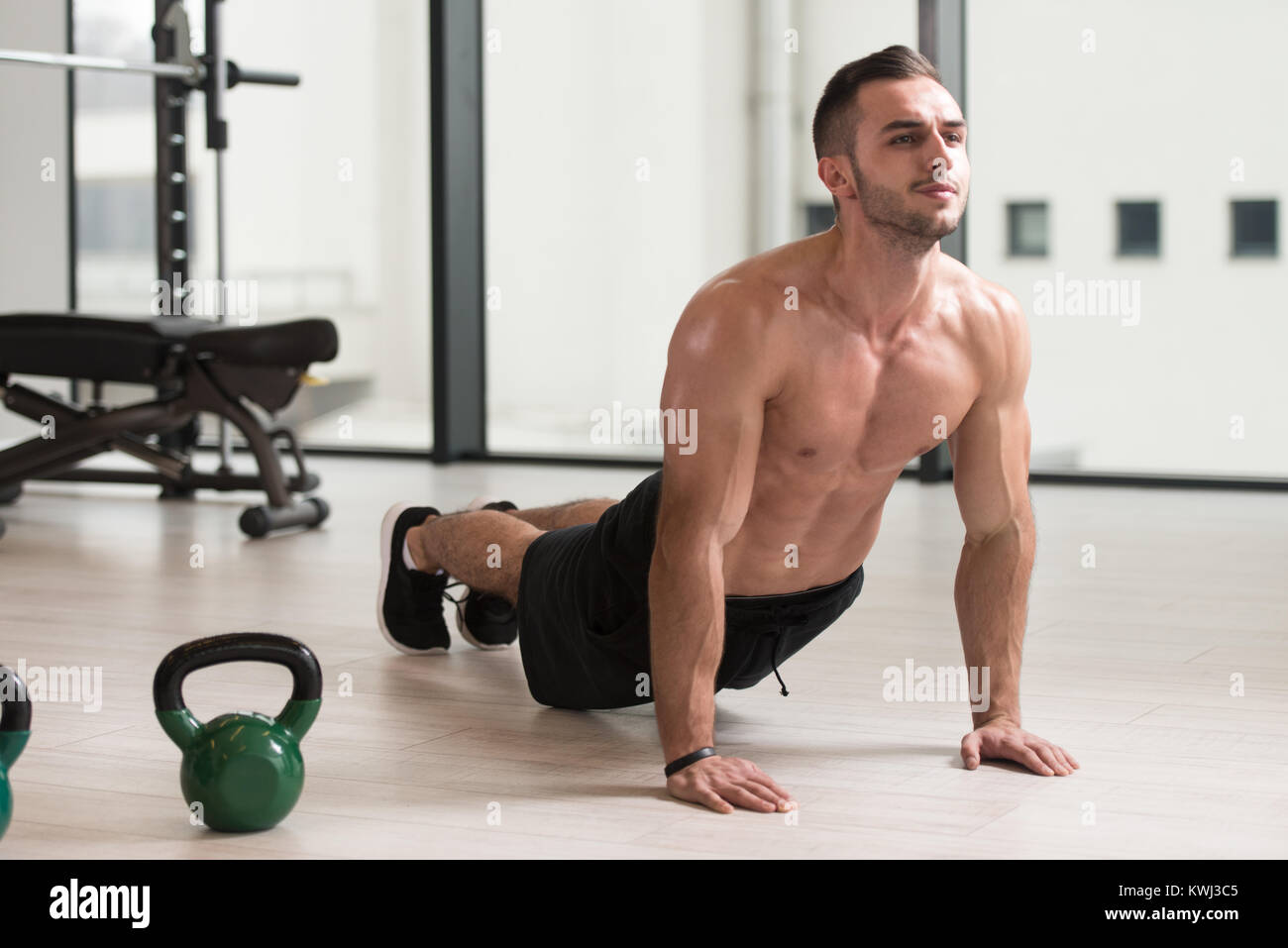 Muscular Man Stretches At The Floor In A Gym And Flexing Muscles ...